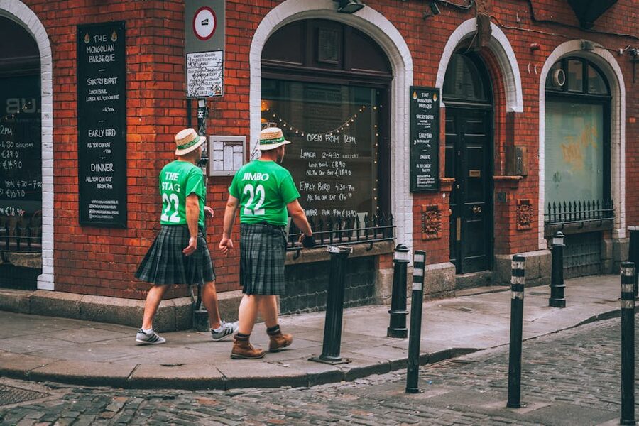 Two men in green jerseys and kilts walking past a restaurant in Dublin
