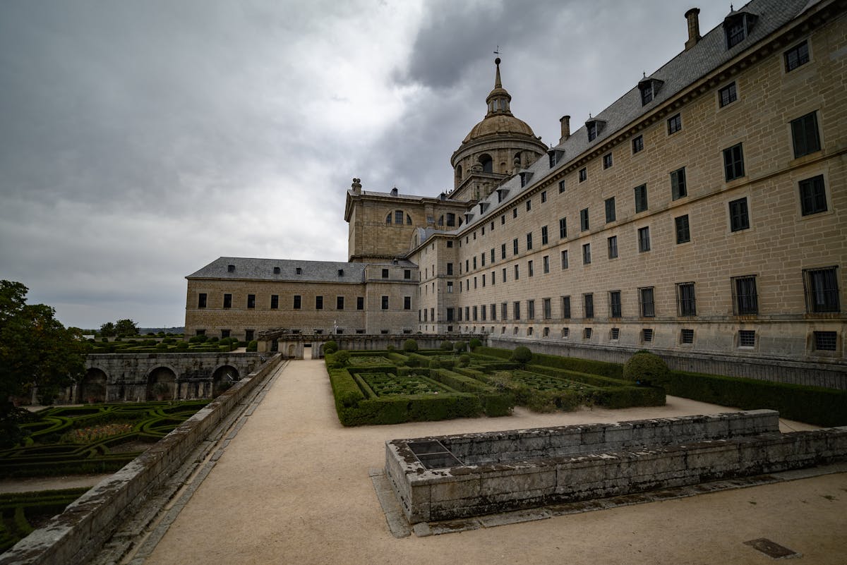 Dramatic view of El Escorial monastery and gardens under cloudy sky
