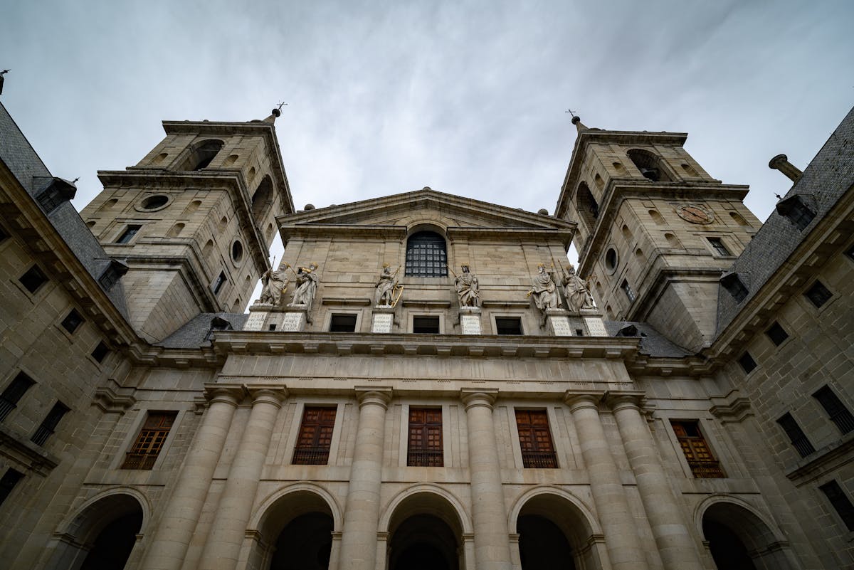 Low-angle view of El Escorial facade under cloudy sky