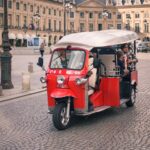 Red tuk tuk with tourists in a European square