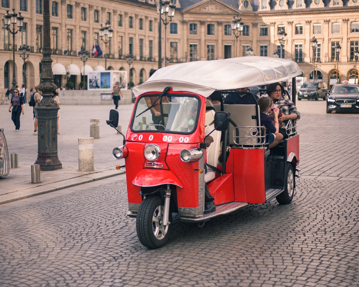 Red tuk tuk with tourists in a European square