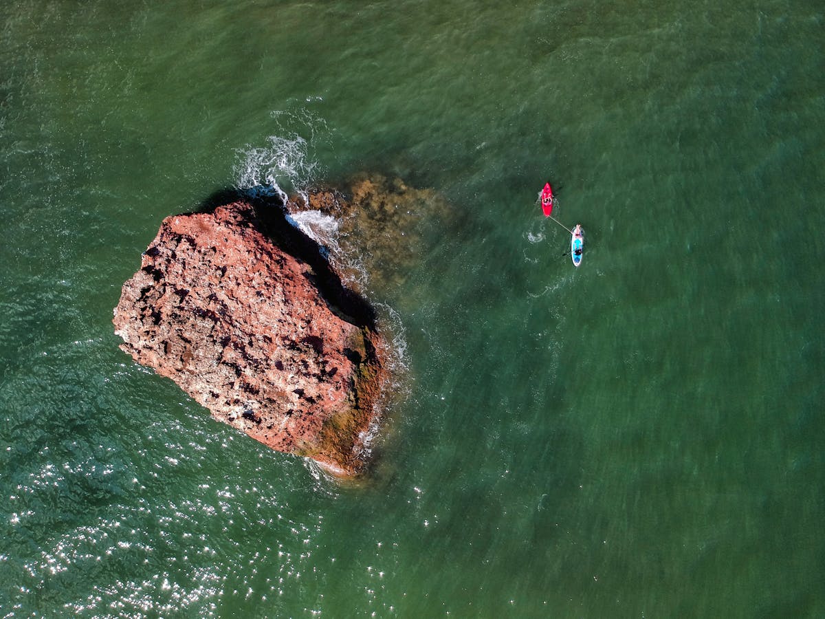 Aerial shot of kayakers paddling near rock formations in green coastal waters