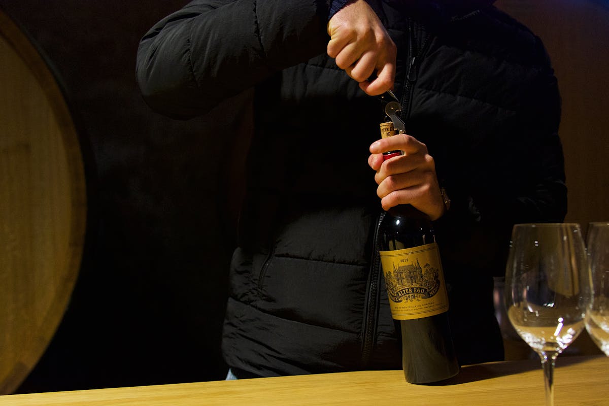 Person uncorking a wine bottle during a tasting session in a Margaux cellar in Bordeaux