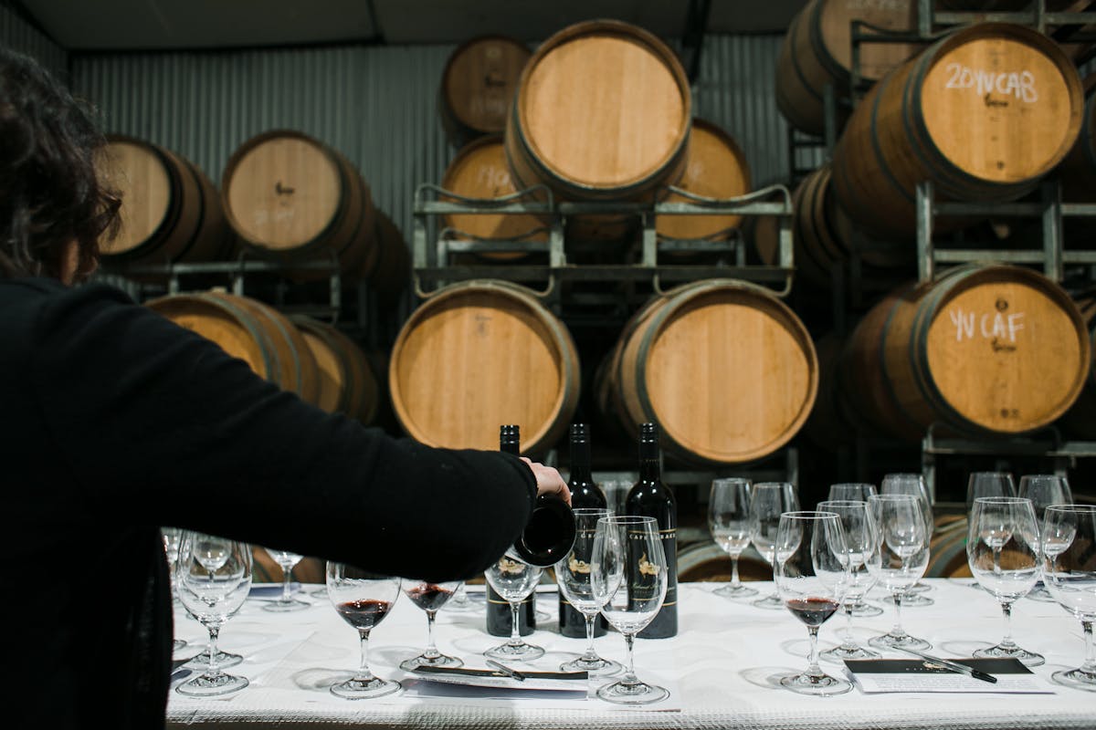 Sommelier pouring red wine from bottle into glass at a barrel-lined winery