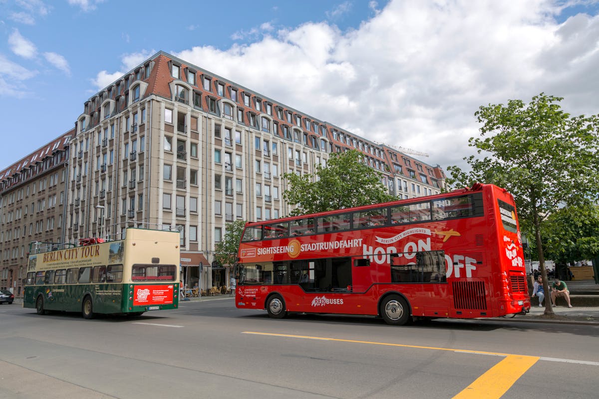 Yellow and red hop-on hop-off sightseeing buses parked near a historic building in Berlin on a sunny day