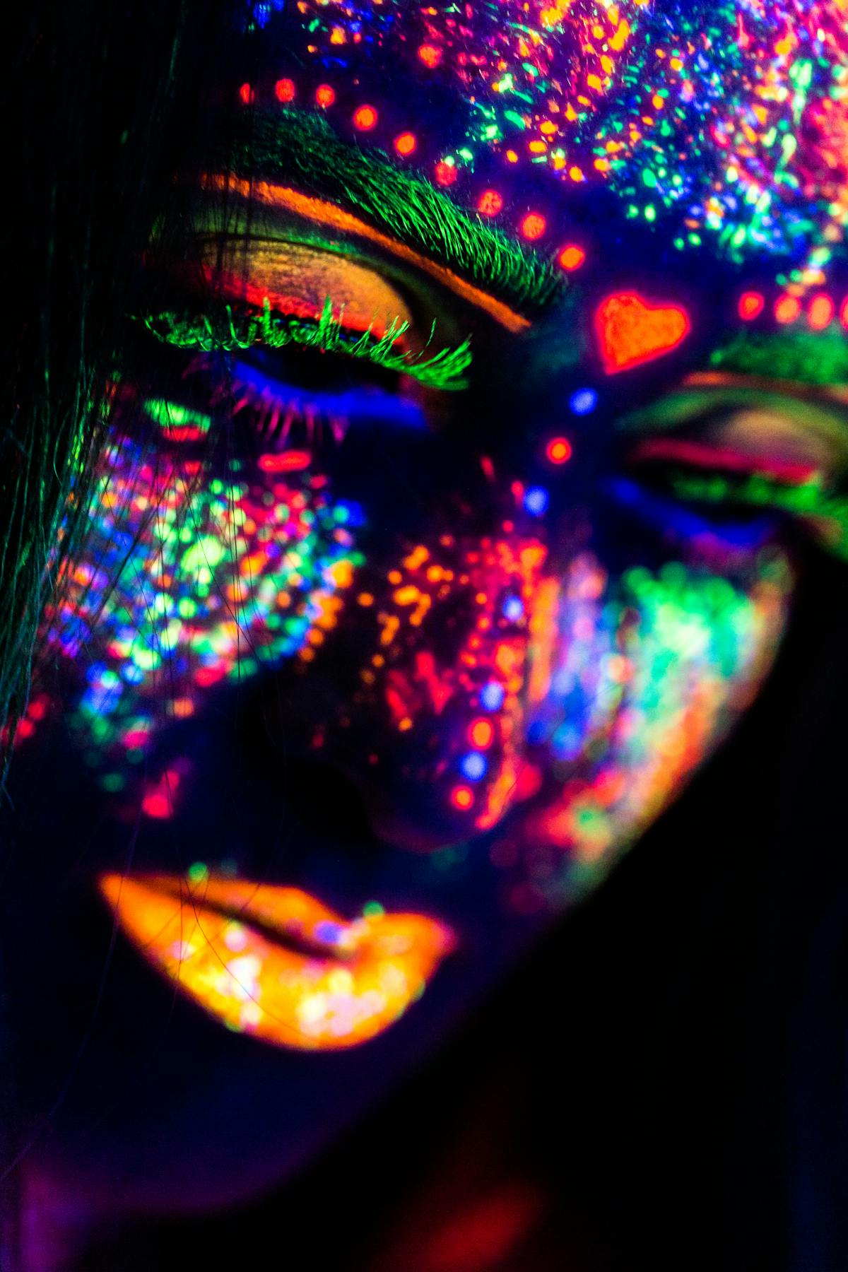 Close-up of a face painted in neon colors glowing under UV light