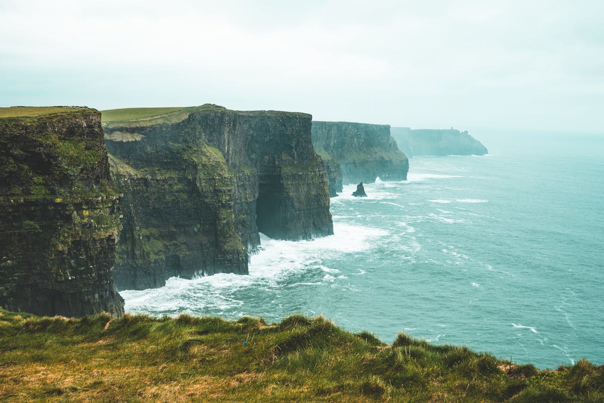 Cliffs of Moher under overcast sky with green grass on top and Atlantic Ocean below