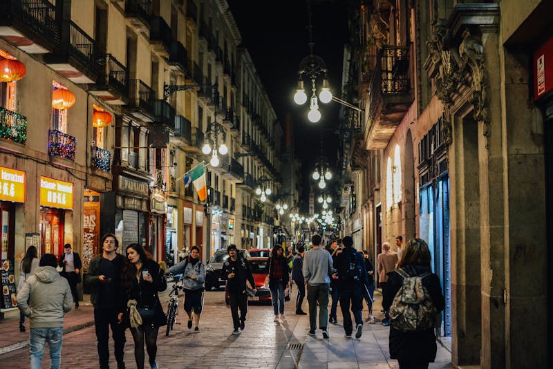 People walking through narrow streets of Barcelona Gothic Quarter at night under warm street lamps