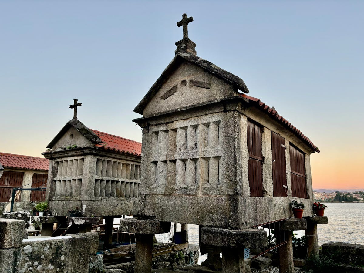 Traditional Galician stone horreo granary structures near water at sunset