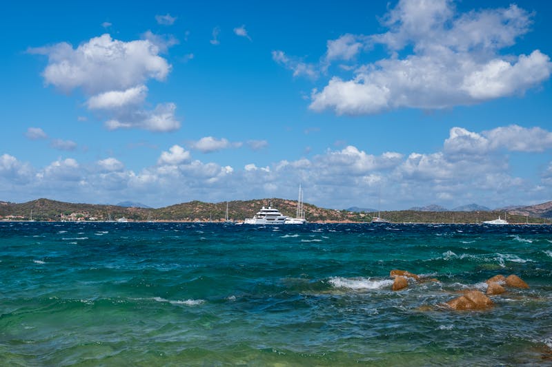 Yachts anchored in a bay along the Sardinian coast with green hills in the background