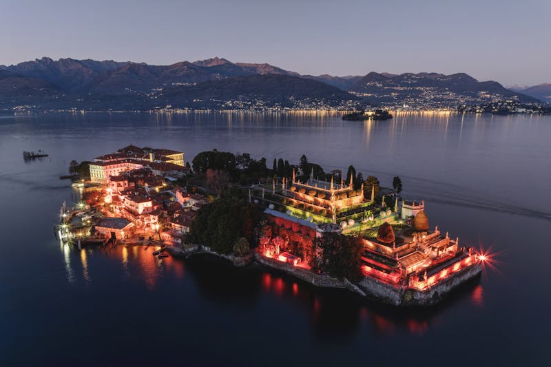 Aerial photograph of Isola Bella lit up at night with Lake Maggiore and mountains in the background