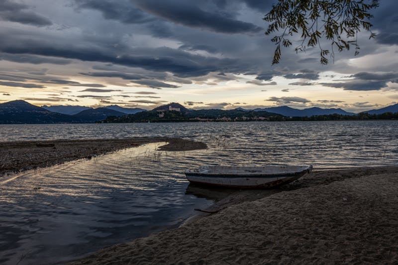 A boat resting by the shores of Lake Maggiore under a dramatic evening sky
