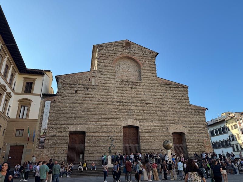 The unfinished stone facade of the Basilica of San Lorenzo in Florence with visitors in the piazza