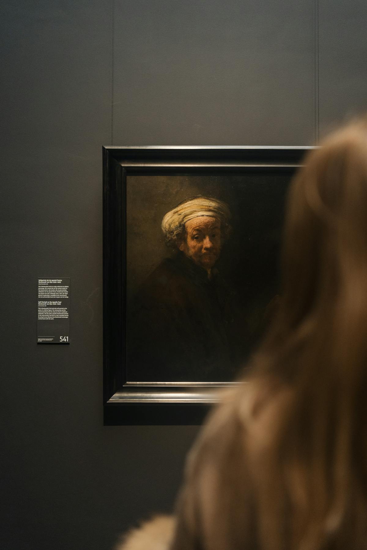 A woman stands before a large classic painting at a museum in Amsterdam