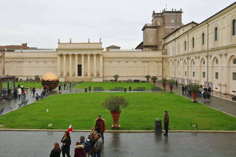 Visitors exploring the Vatican City courtyard beside historic architecture
