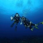 Two scuba divers with gear exploring the deep blue ocean underwater