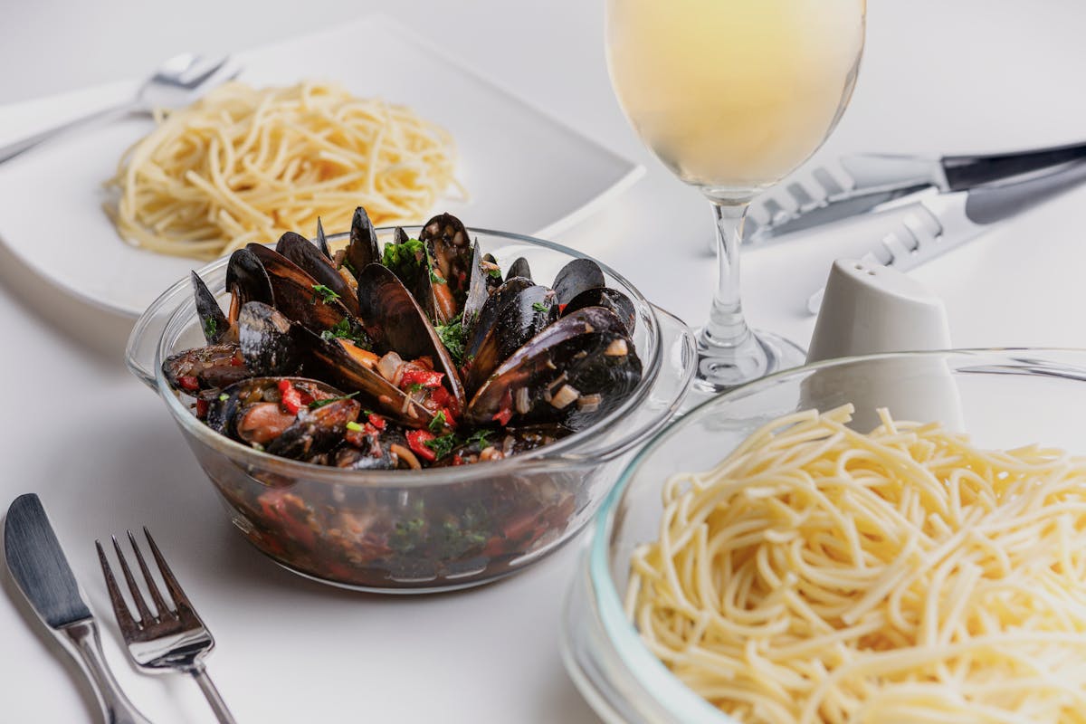 A seafood pasta dish with fresh mussels and a glass of white wine