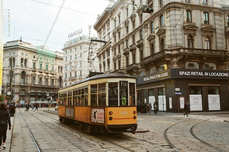 A yellow vintage tram traveling through the streets of Milan with classic architecture in the background