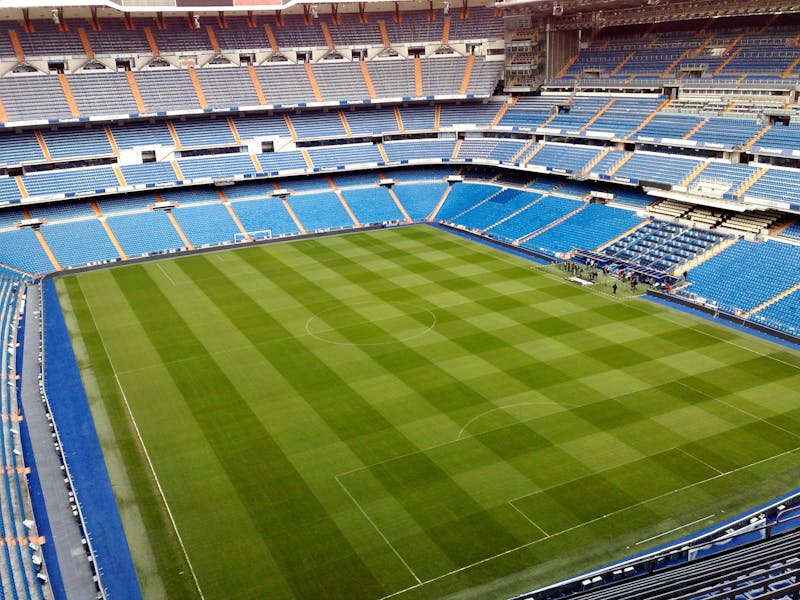 Top-down aerial view of the pristine green pitch and symmetrical blue seating at Santiago Bernabeu