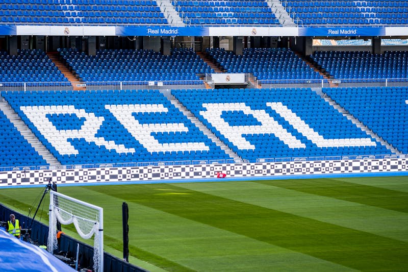 Empty seating area at Santiago Bernabeu with REAL written in white seats against blue background and green pitch