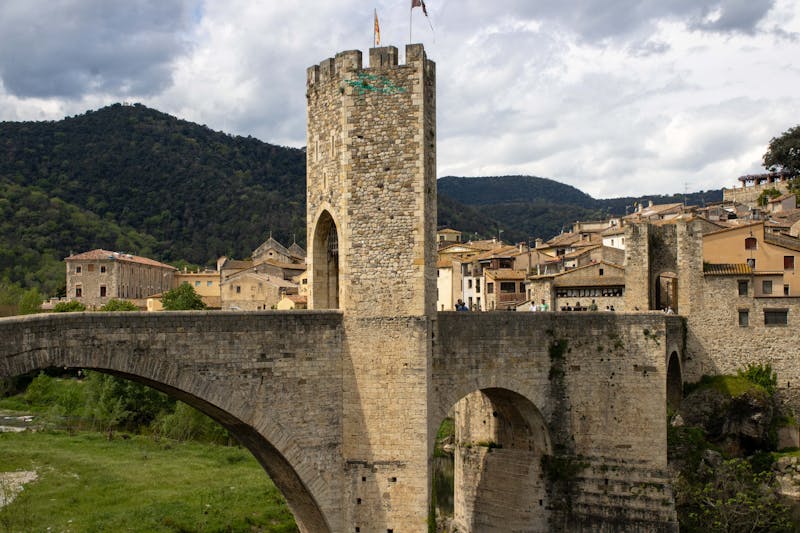 Medieval stone bridge spanning a river with an old Catalan town in the background