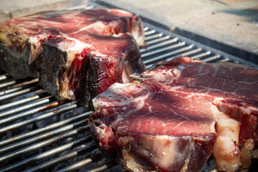 Large T-bone steaks grilling over hot coals in the traditional Florentine style