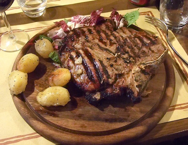 A thick cut bistecca alla fiorentina T-bone steak being grilled in a Florence restaurant
