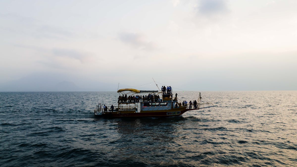 Silhouetted boat carrying passengers on calm ocean waters during twilight