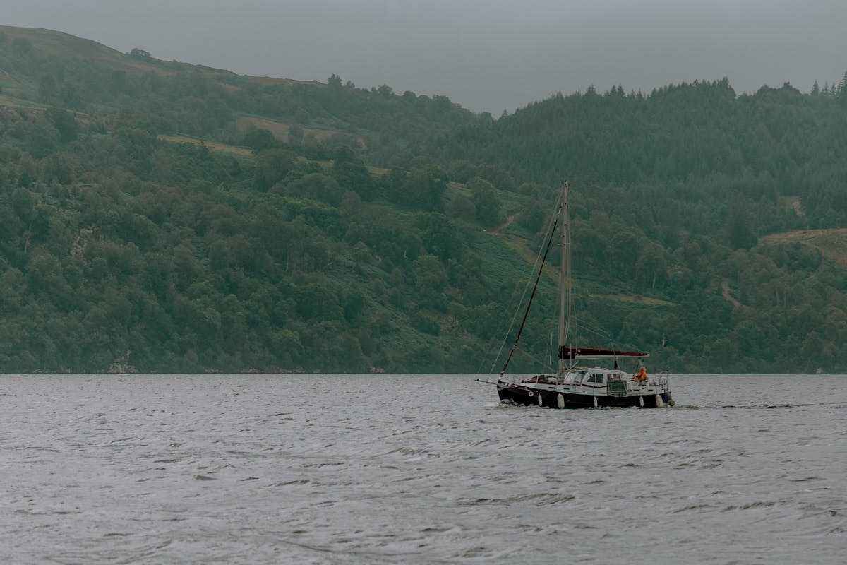 A small boat sailing across the calm dark waters of Loch Ness with the green hillside of the Scottish Highlands in the background