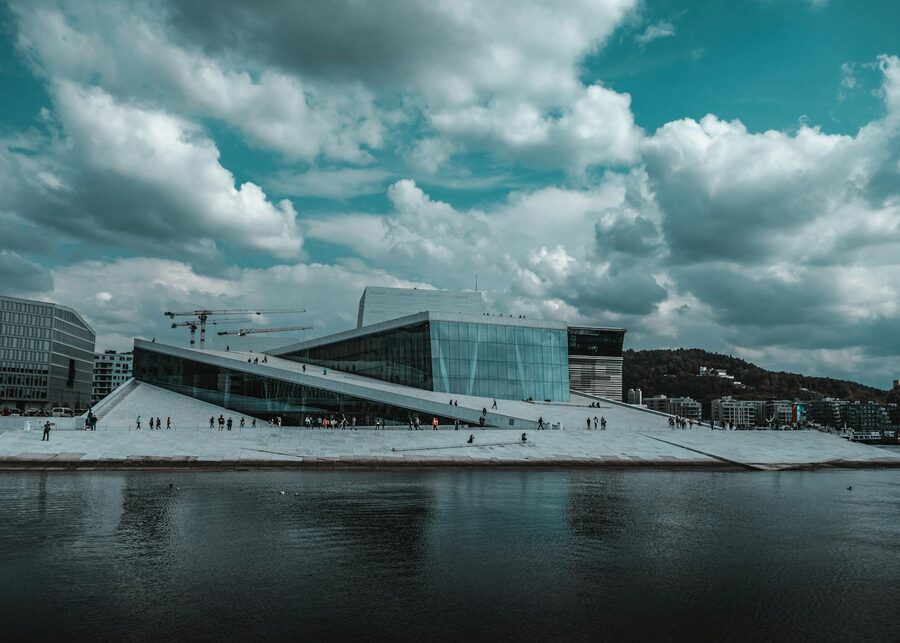The modern Oslo Opera House with dramatic clouds and waterfront reflection in Oslo, Norway.