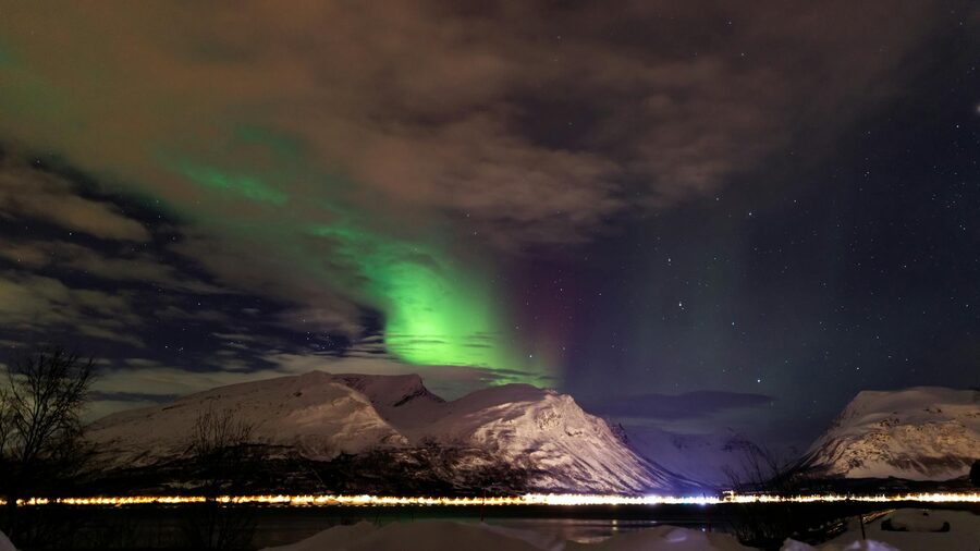 Capture of vibrant Northern Lights illuminating snowy mountains against a starry night sky.