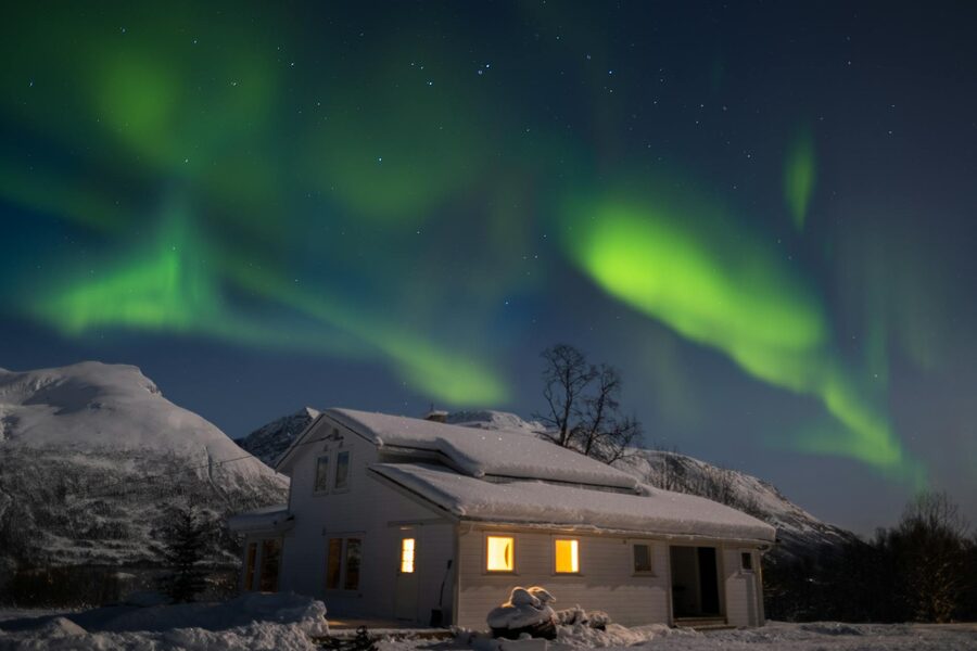 Stunning aurora borealis illuminates the night sky over a snow-covered house in Tromsø, Norway.