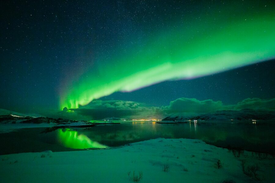 Stunning aurora borealis illuminating the night sky in Tromsø, Norway, reflecting on snowy landscape