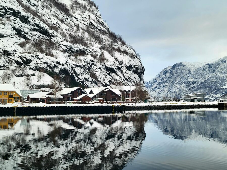 Serene winter scene of a snowy village with fjord reflections in Flåm, Norway.