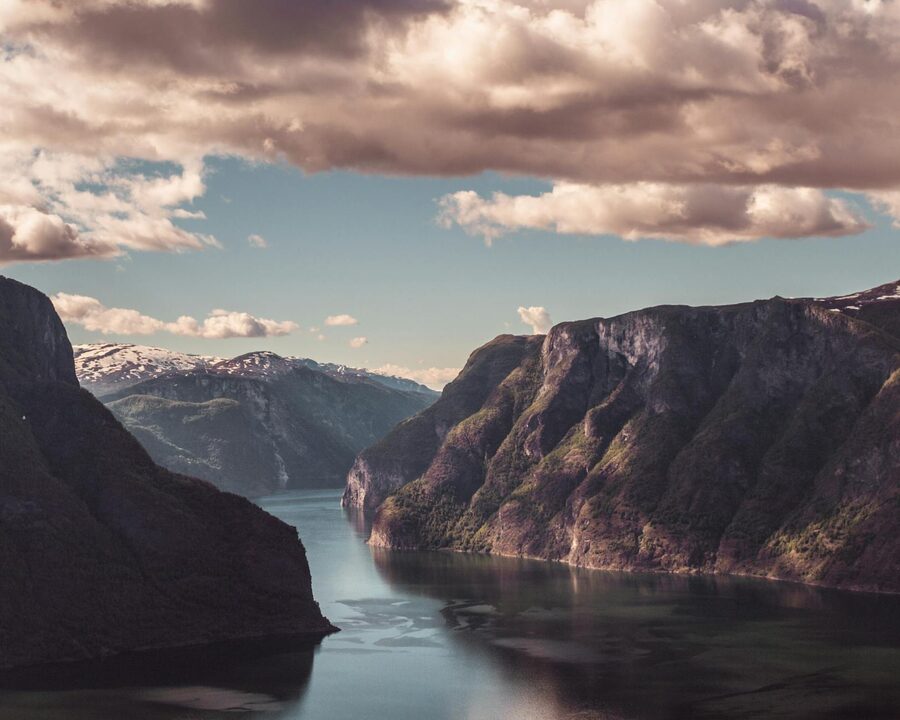 Tranquil Aurlandsfjord at sunset in Flåm, Norway, with majestic mountains and a serene sky.