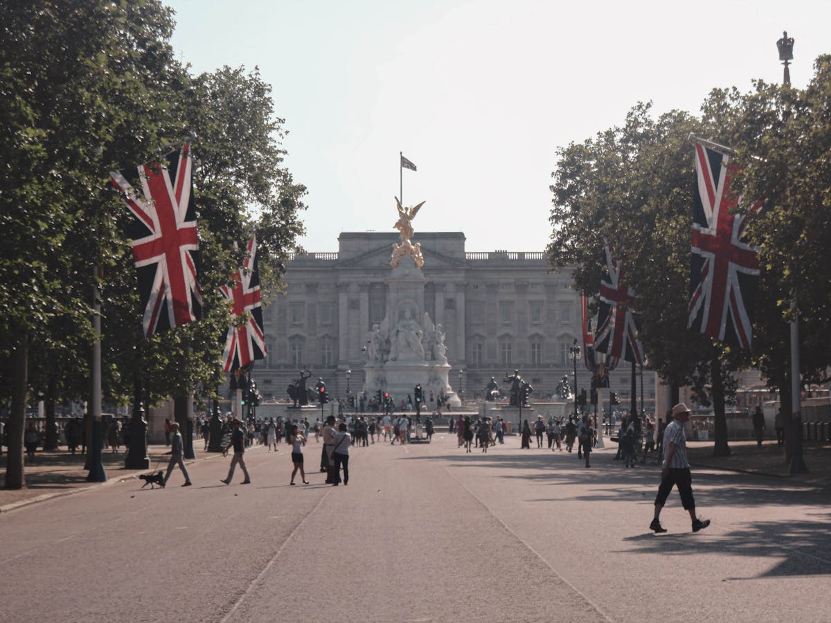 A vibrant day at Buckingham Palace with Union Jack flags lining the approach and travelers exploring the grounds