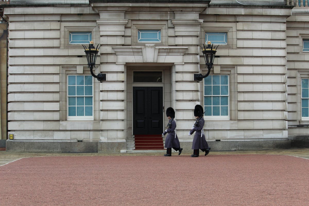 Two royal guards in traditional red uniform and bearskin hats marching at Buckingham Palace London