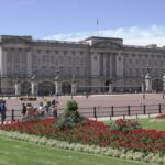 View of Buckingham Palace facade with lush green gardens in the foreground on a clear sunny day