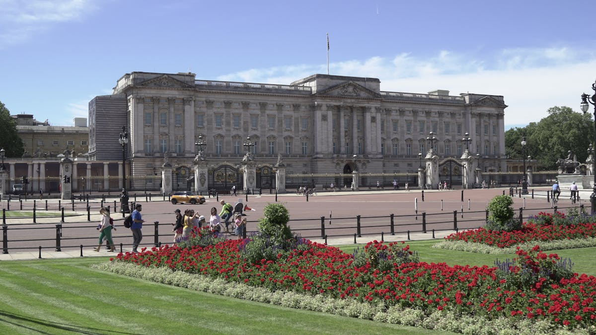 View of Buckingham Palace facade with lush green gardens in the foreground on a clear sunny day