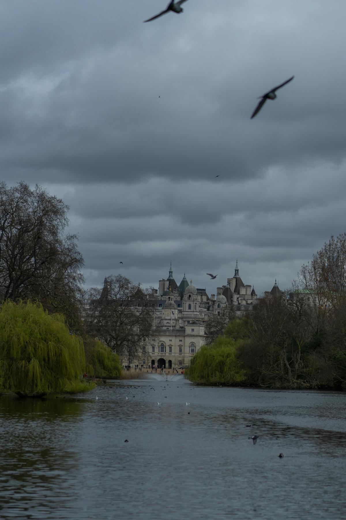 A tranquil view of St James Park with a historic building in the background under cloudy skies London