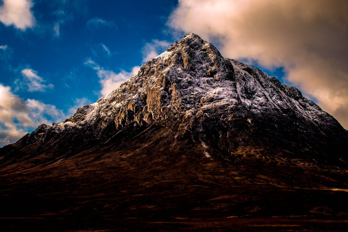 The snow-capped pyramid-shaped peak of Buachaille Etive Mor in Glencoe Scotland under dramatic dark clouds