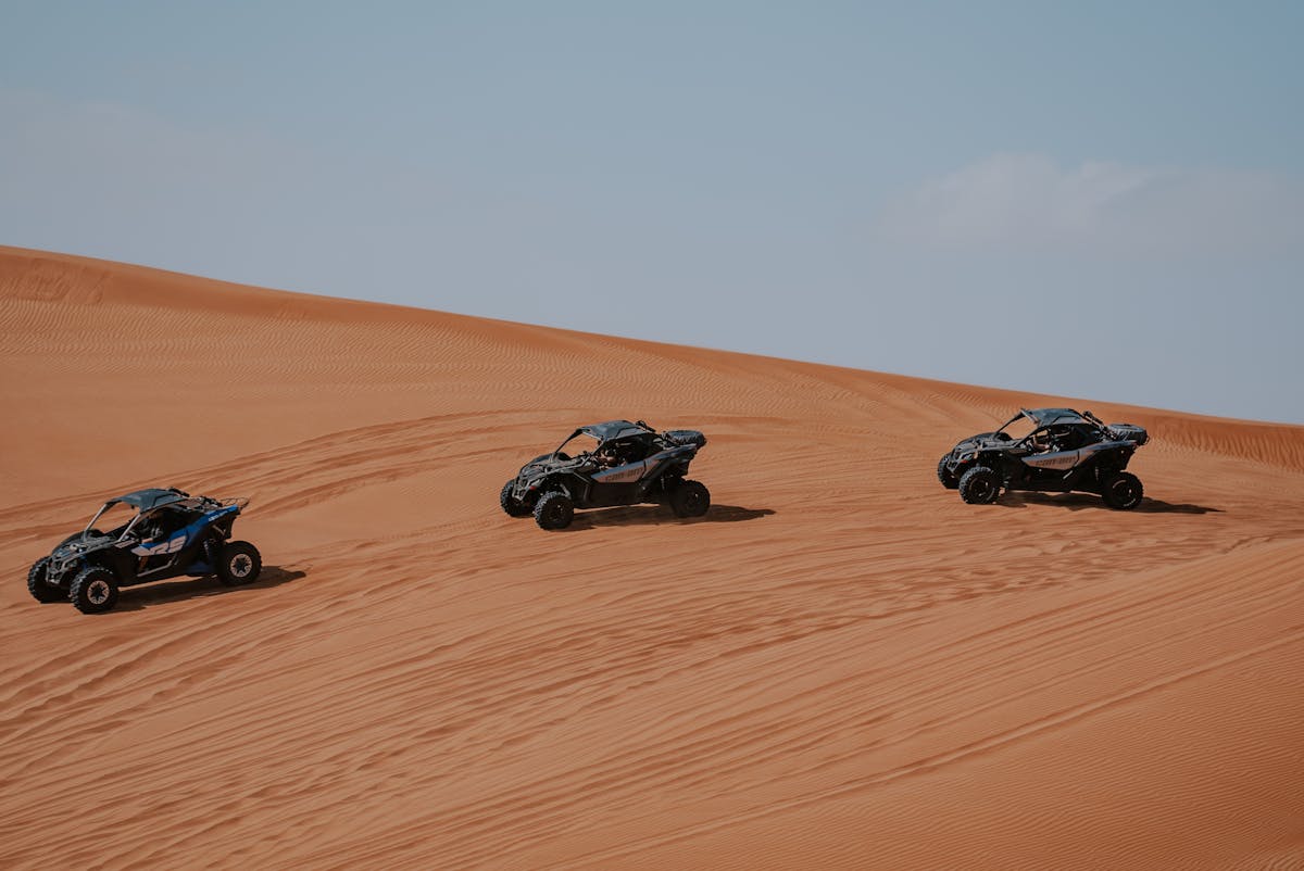 Three all-terrain vehicles racing across expansive desert sand dunes