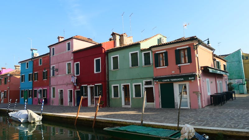 Colorful houses lining a canal in Burano, Venice, Italy, under a clear blue sky