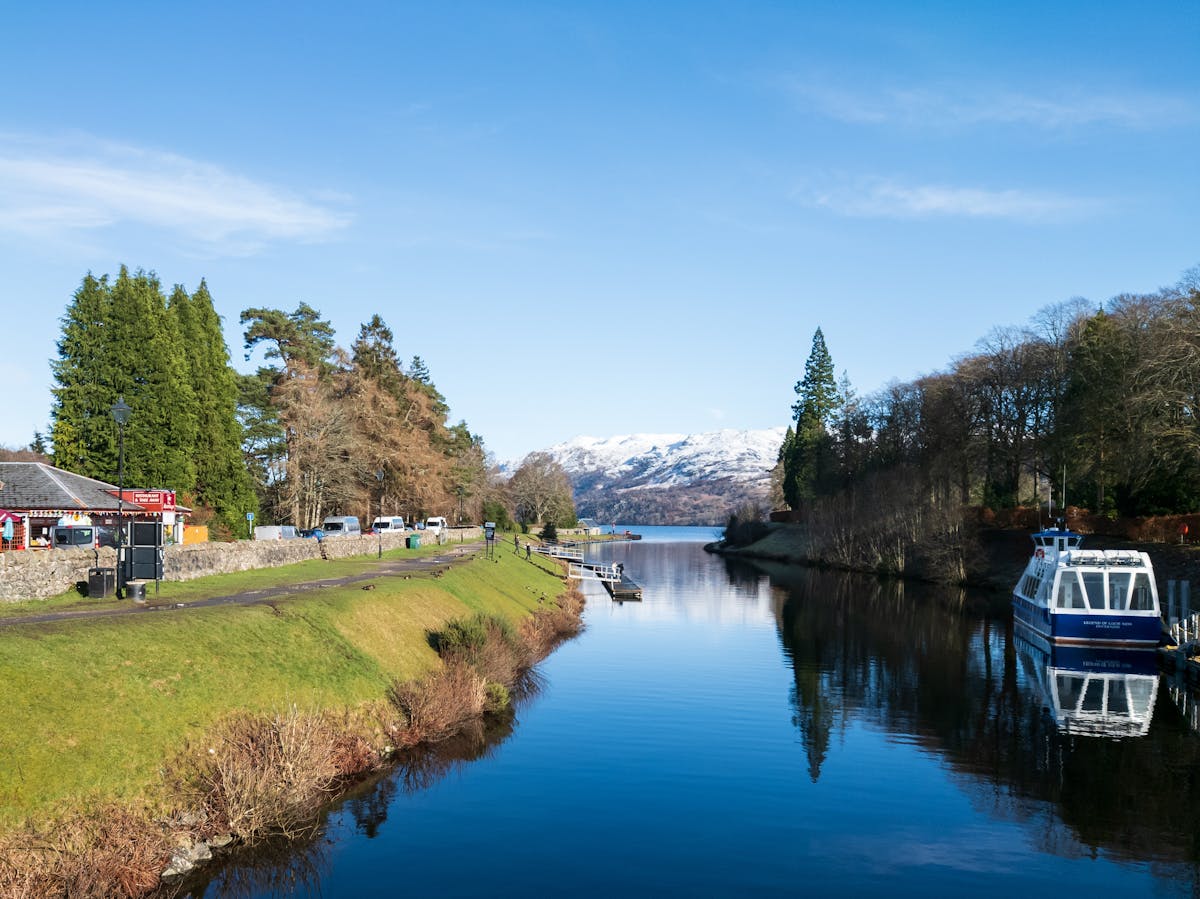 A peaceful view of the Caledonian Canal with a boat surrounded by greenery and hills near Fort Augustus in Scotland