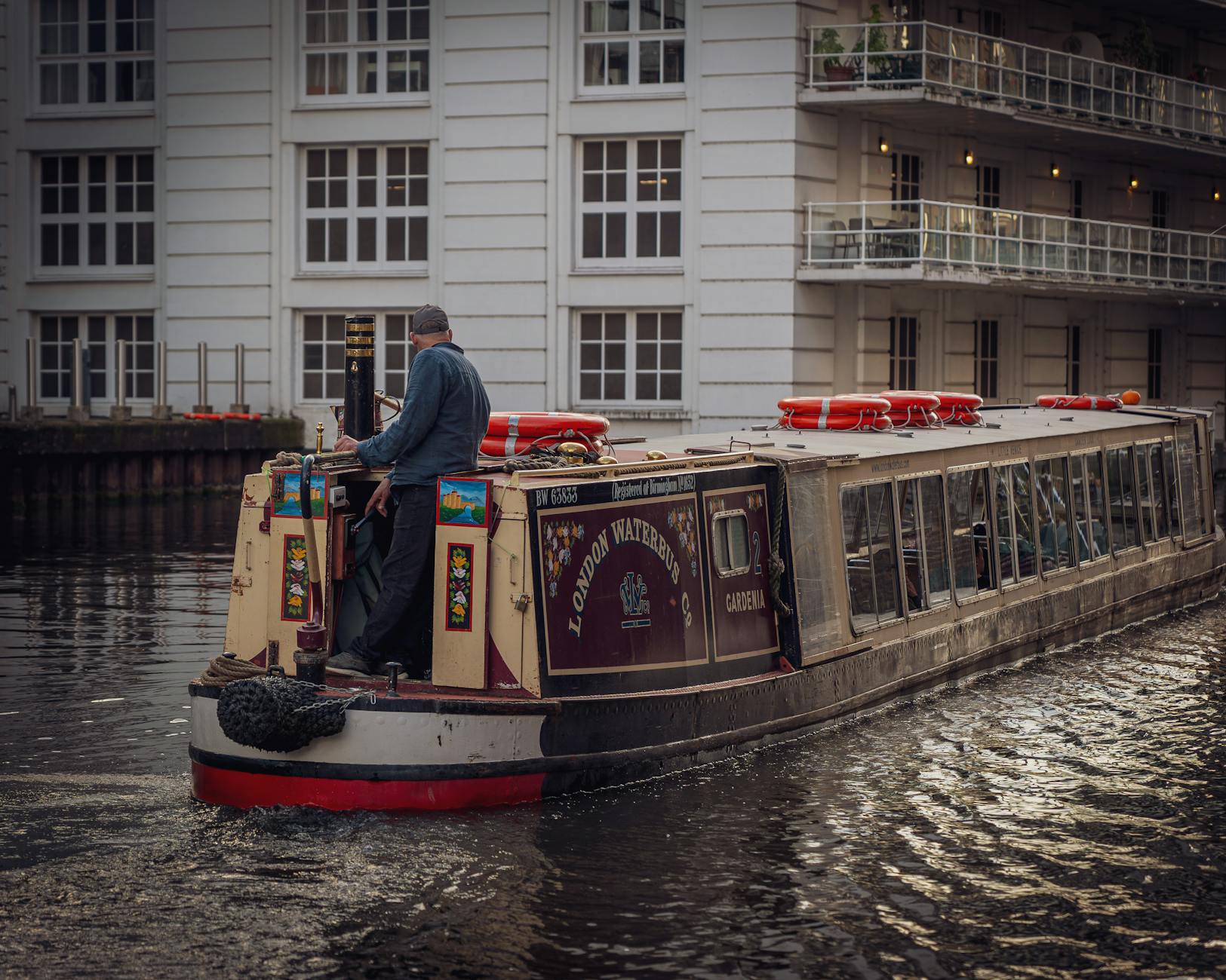 A canal boat cruises past modern apartment buildings along an urban waterway