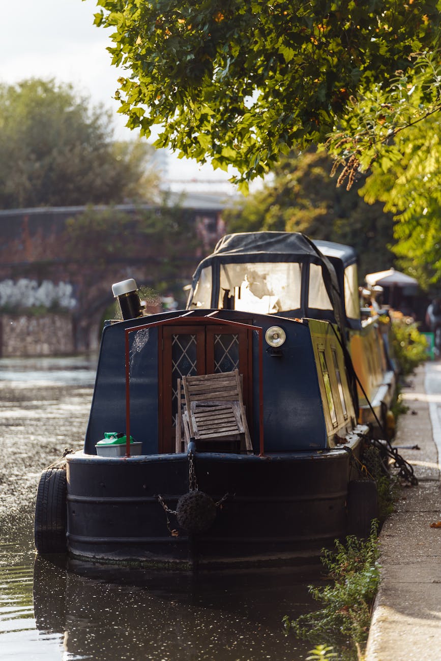 A green narrowboat moored on a still canal surrounded by trees and towpath