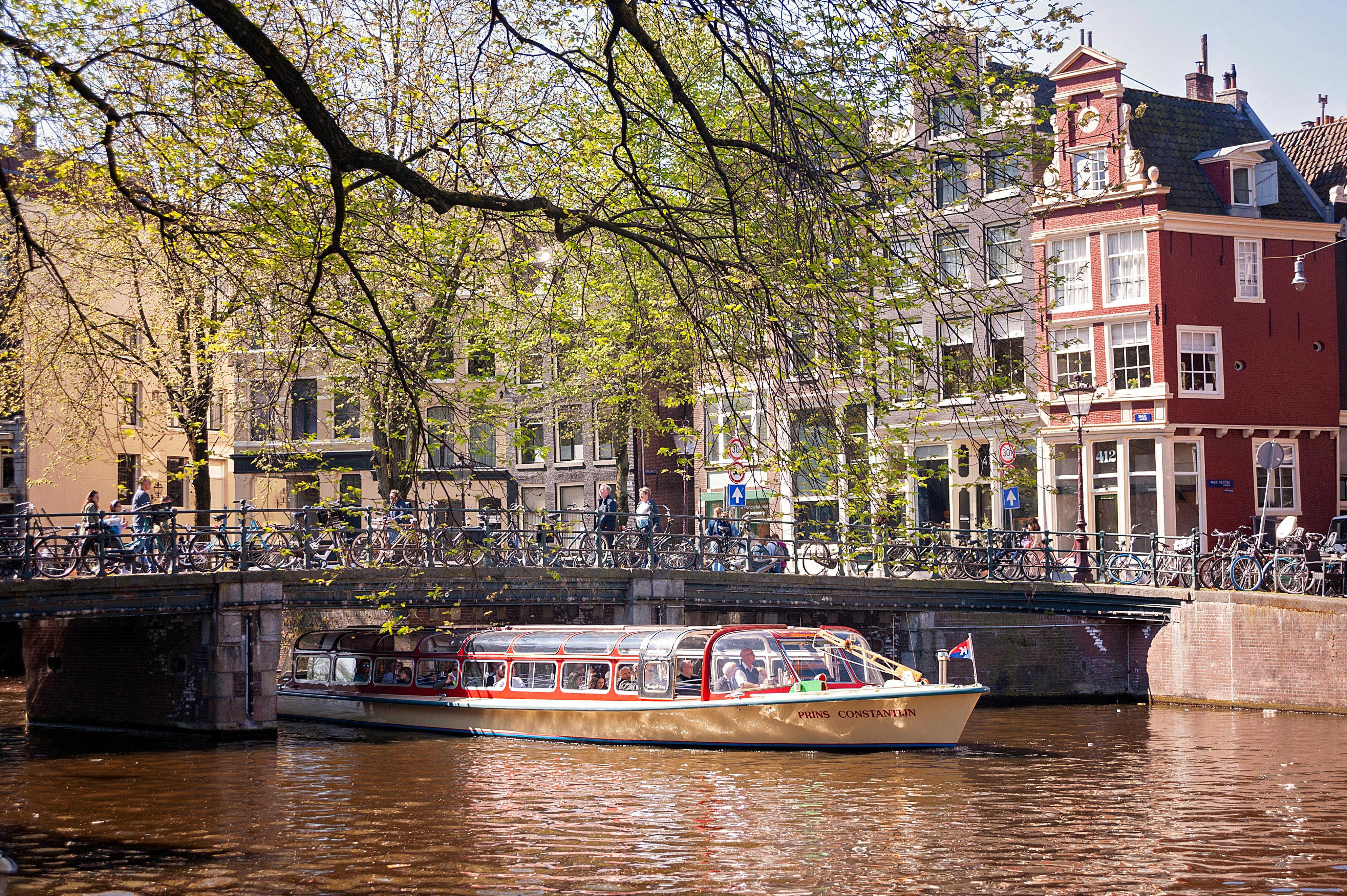 Tour boat cruising along Amsterdam canal with Dutch buildings and bridge