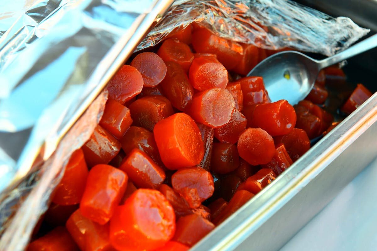 Glazed marinated carrots in a stainless steel tray with serving spoon