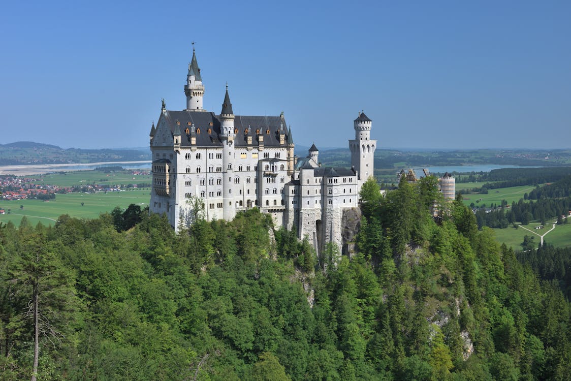 Castle perched on a forested hill in the German Alps with mountain peaks behind