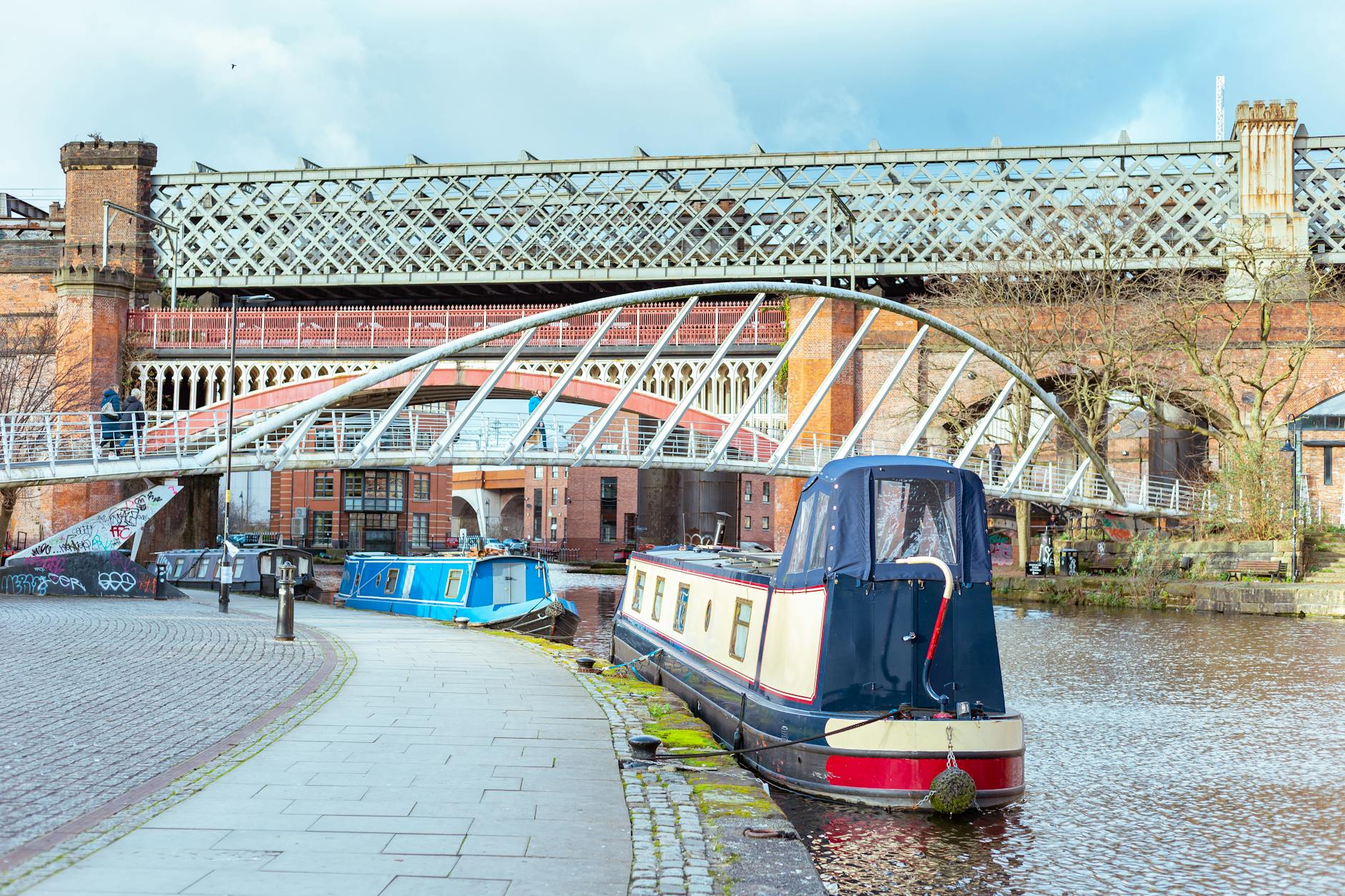 Colourful canal boats lined up at Castlefield Basin with historic bridges behind